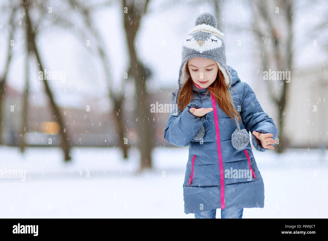 Funny little girl having fun in beautiful winter park during snowfall ...
