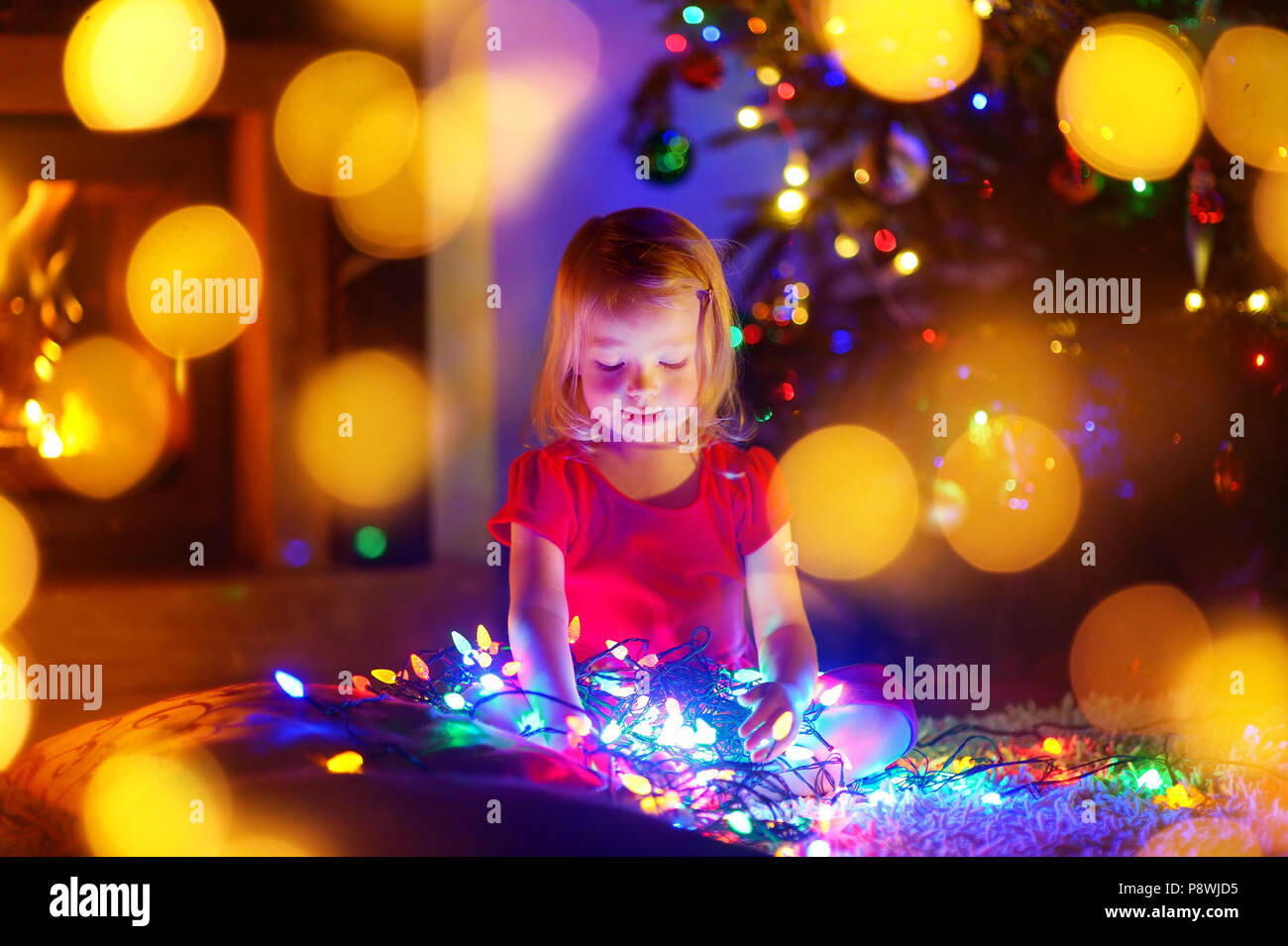 Adorable little girl playing with Christmas lights by a fireplace in ...