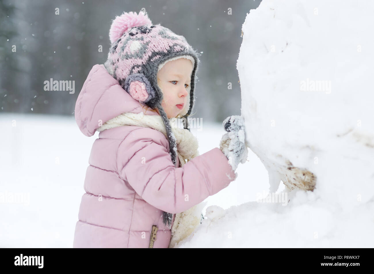 Funny little girl having fun in beautiful winter park during snowfall ...
