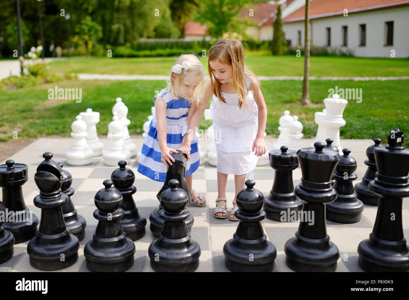 Two little sisters playing giant chess outdoors Stock Photo - Alamy