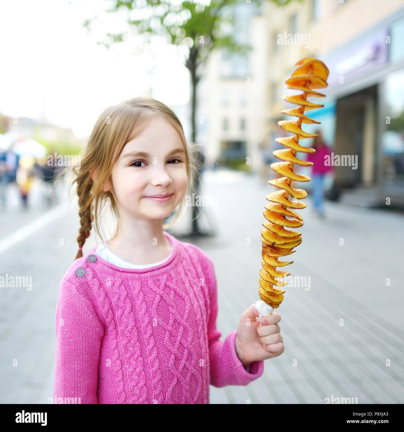 Cute little girl eating fried potato on a stick on warm summer day ...