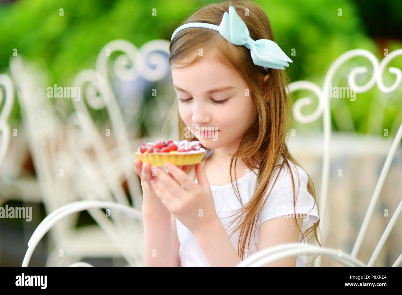 Adorable little girl eating fresh sweet strawberry cake outdoors on ...