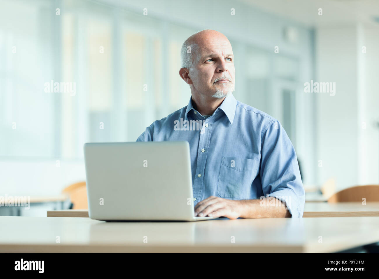 Business man seated in front of laptop computer while looking off in ...
