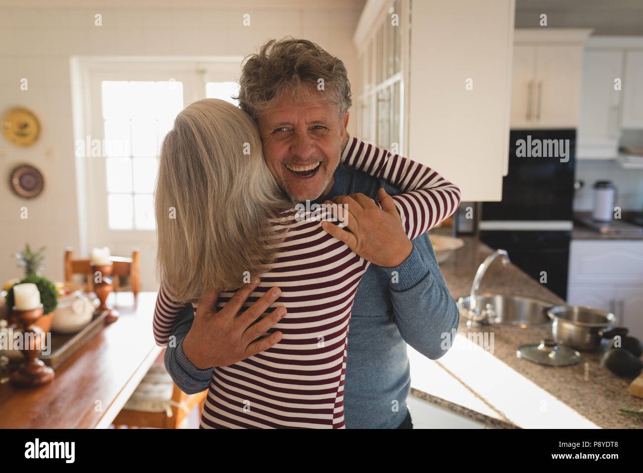 Senior couple hugging in the kitchen Stock Photo - Alamy