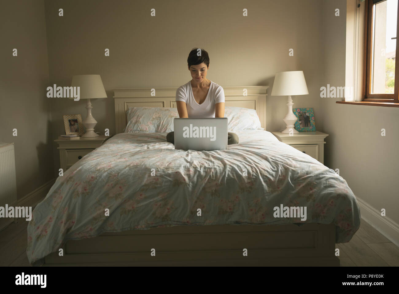 Woman using laptop on bed in bedroom Stock Photo - Alamy