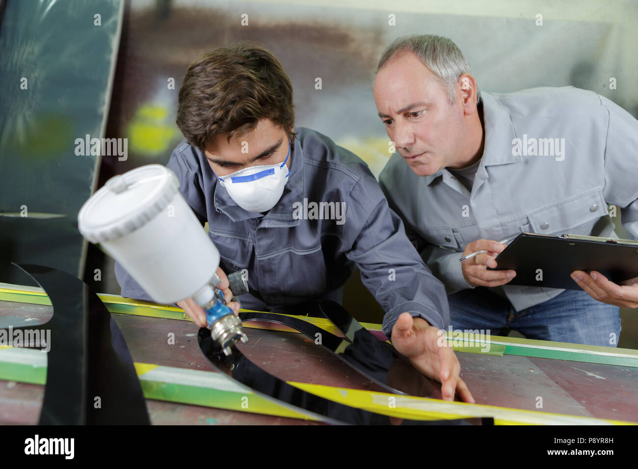 apprentice and worker painting with spray gun Stock Photo - Alamy
