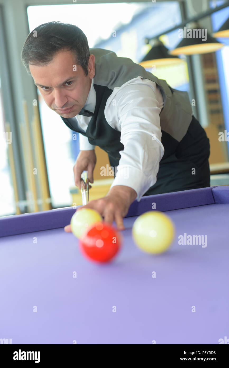 young professional man playing billiards in the dark billiard club ...