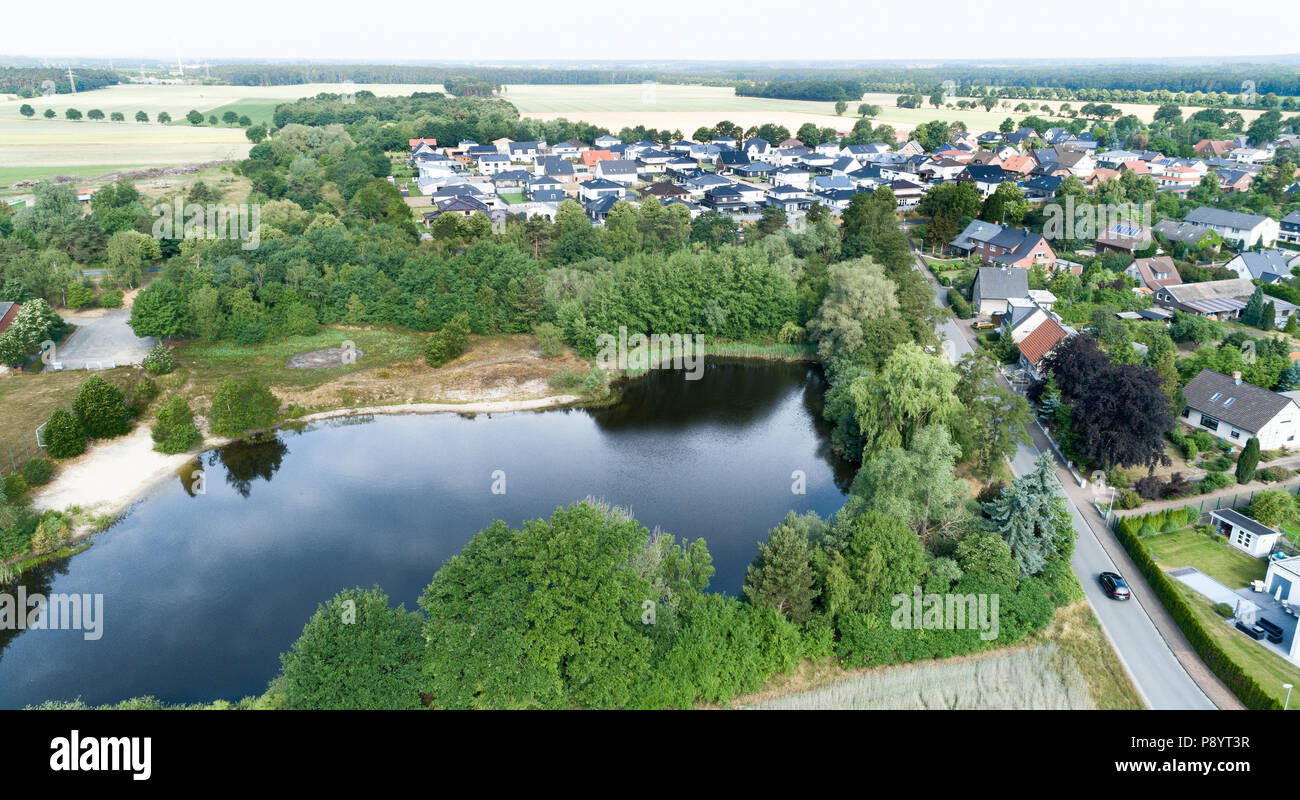 Aerial view of a suburb behind a small lake and a wooded area, with ...