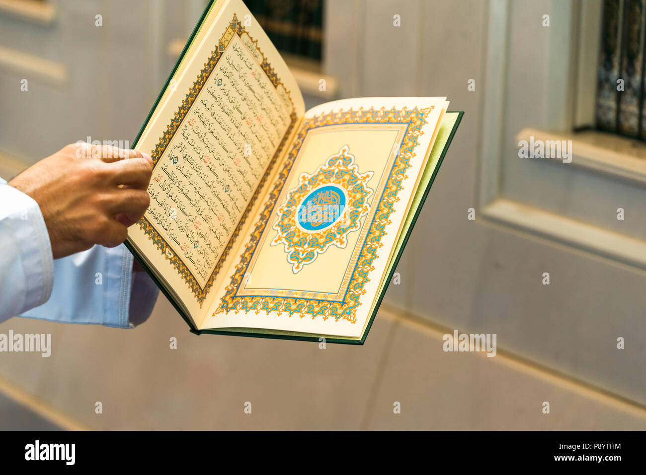 Copy of the holy Quran held by the hands of a man in the white interior ...