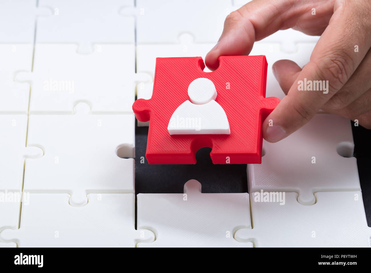 Close-up of a person's hand placing red human figure piece into jigsaw ...
