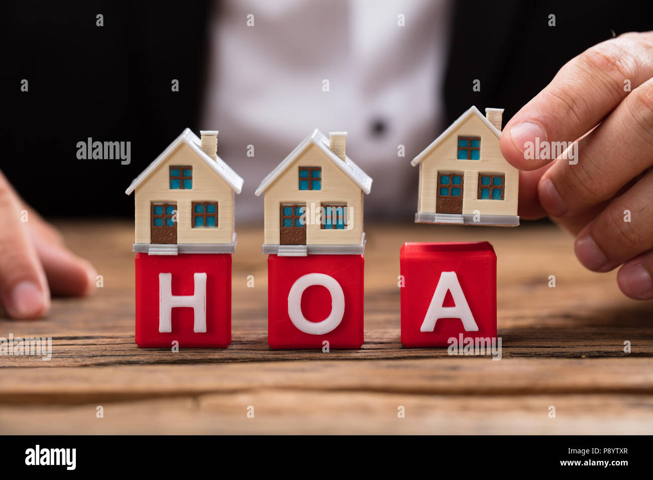 Businessperson's hand placing house model over red HOA blocks on wooden ...