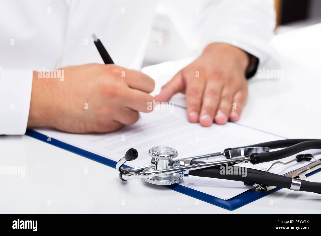 Doctor's hand signing document with stethoscope on desk Stock Photo - Alamy