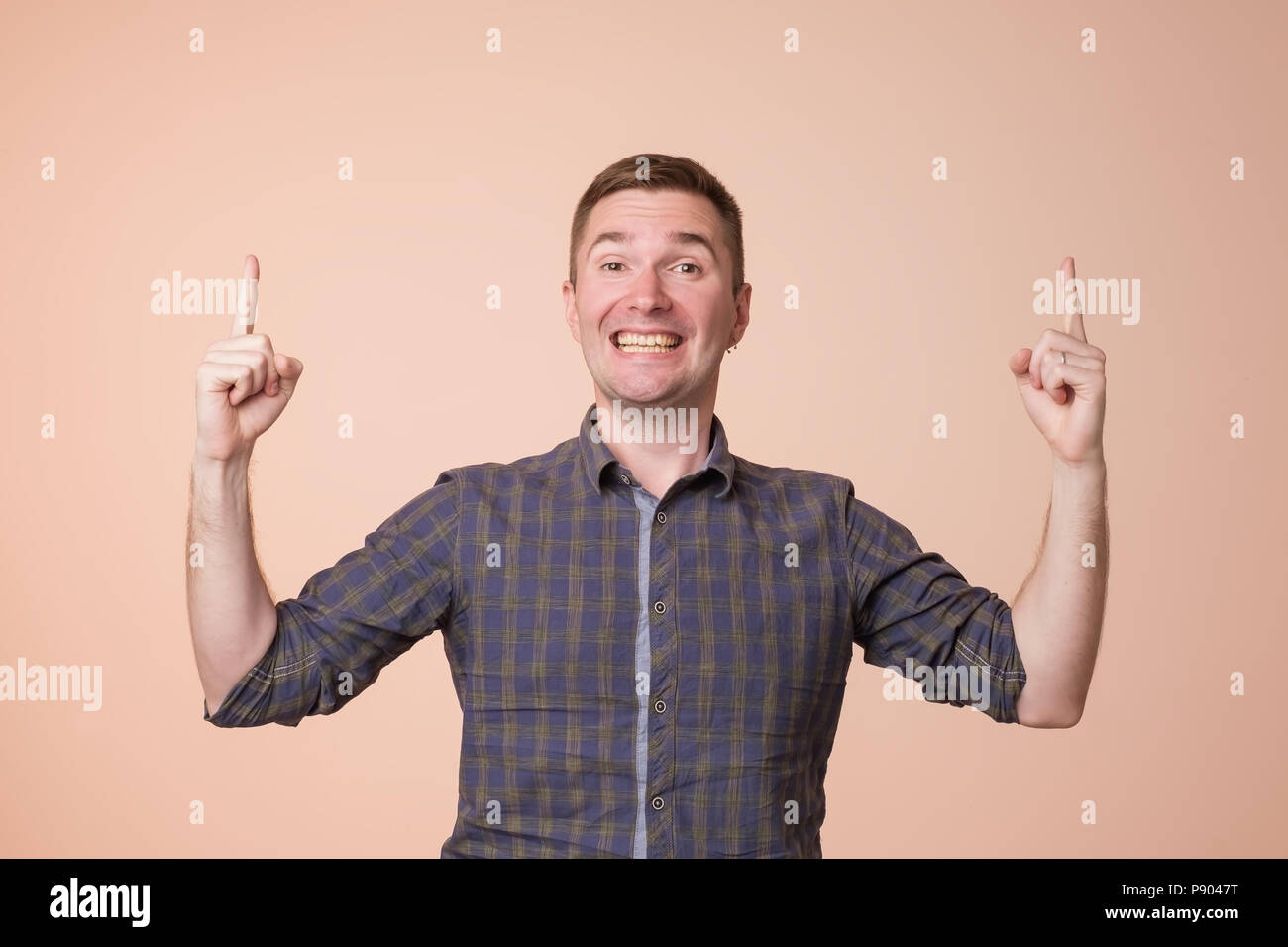 Surprised young man pointing up with two hands. Hey look up concept ...