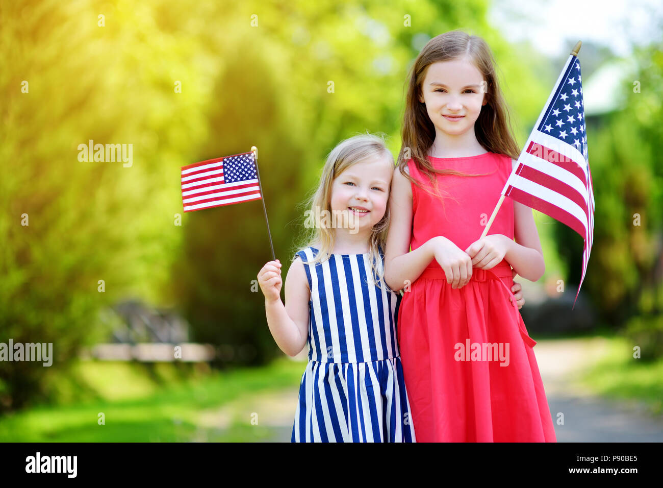 Two adorable little sisters holding american flags outdoors on ...