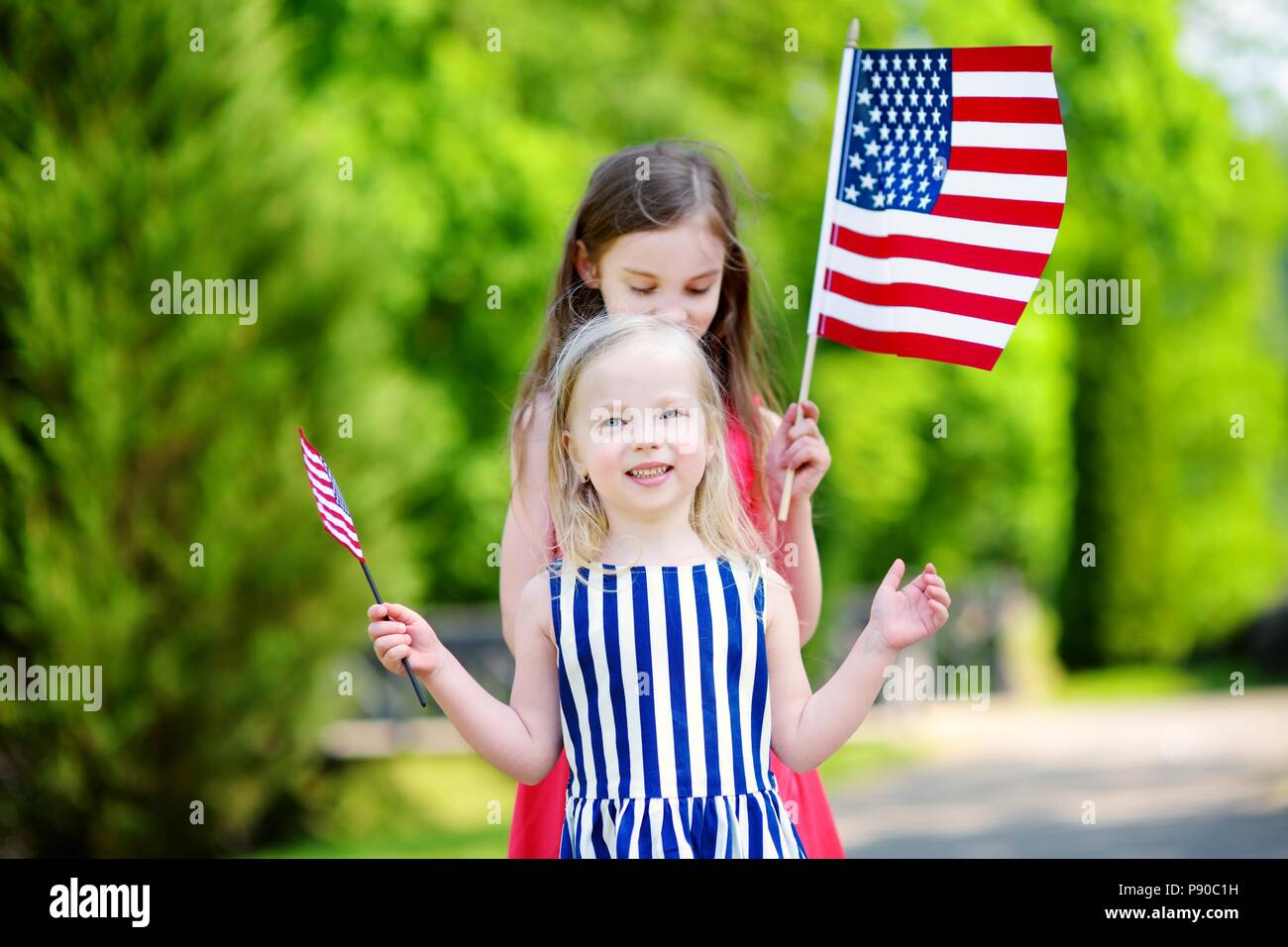 Two adorable little sisters holding american flags outdoors on ...