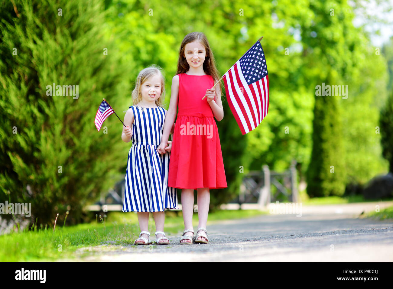 Two adorable little sisters holding american flags outdoors on ...