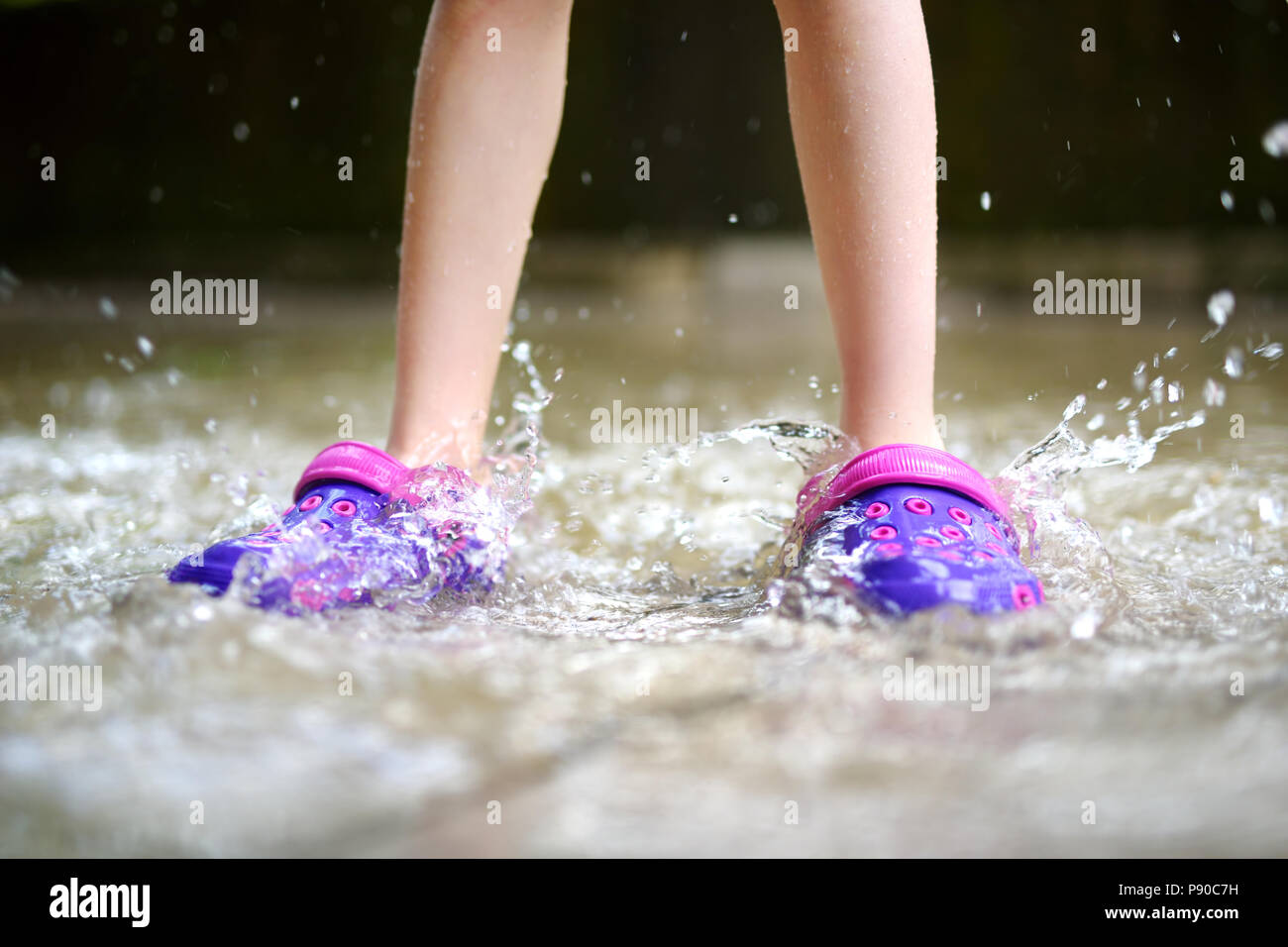 Child wearing rubber shoes jumping into a puddle on warm summer day ...