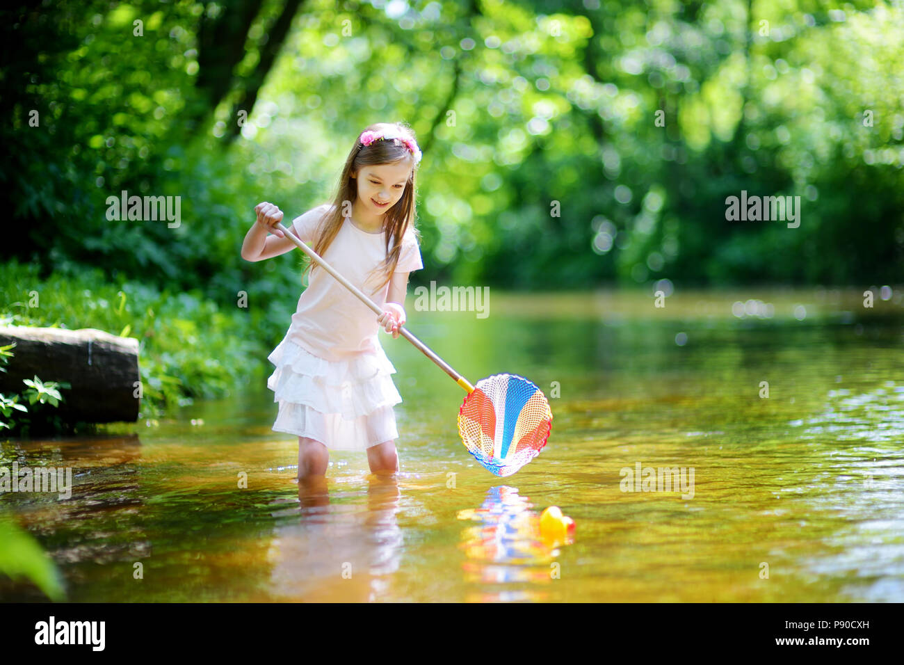 Cute little girl playing in a river catching rubber ducks with her ...
