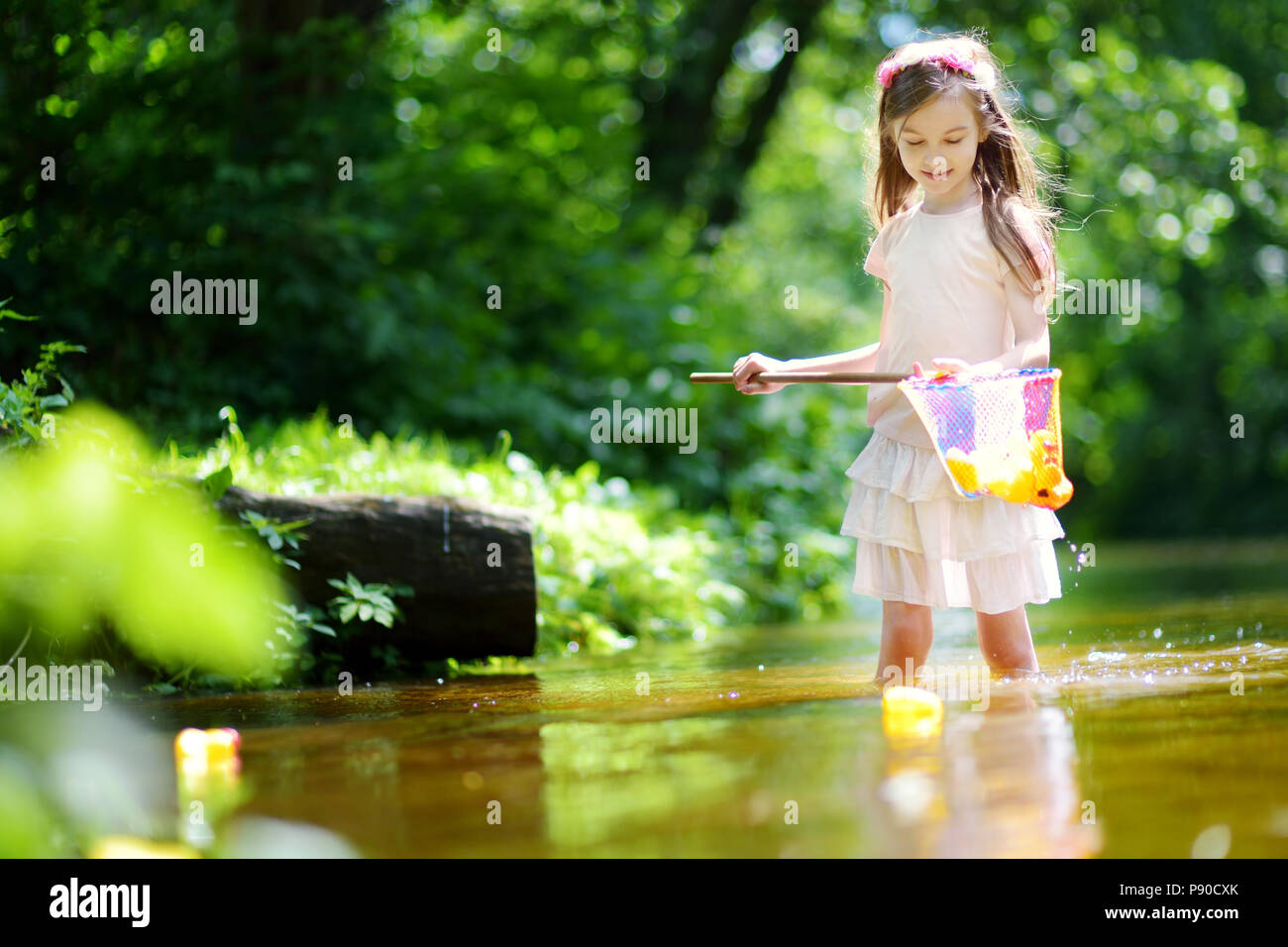 Cute little girl playing in a river catching rubber ducks with her ...