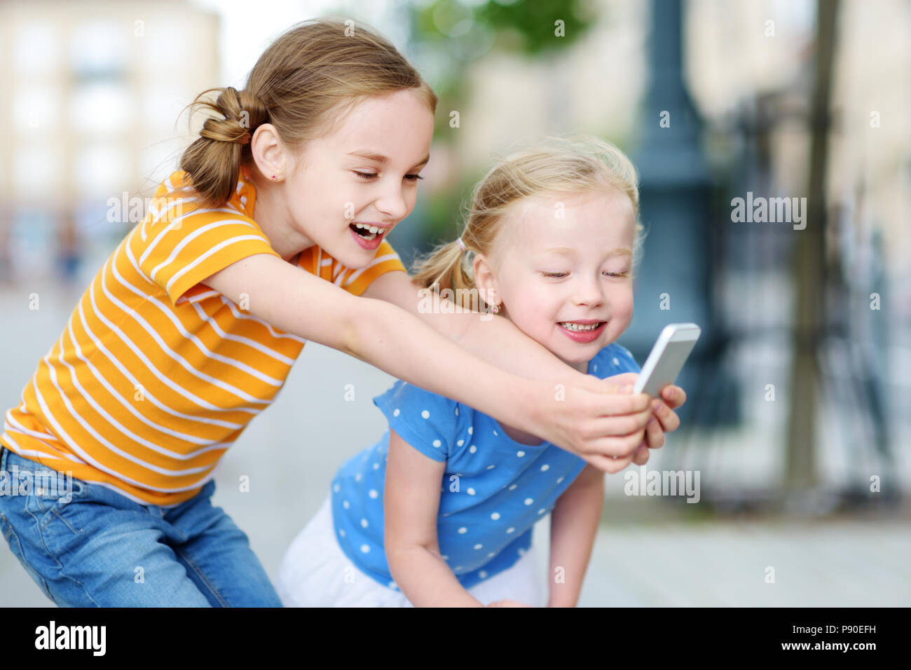 Two cute little sisters playing outdoor mobile game on their smart ...