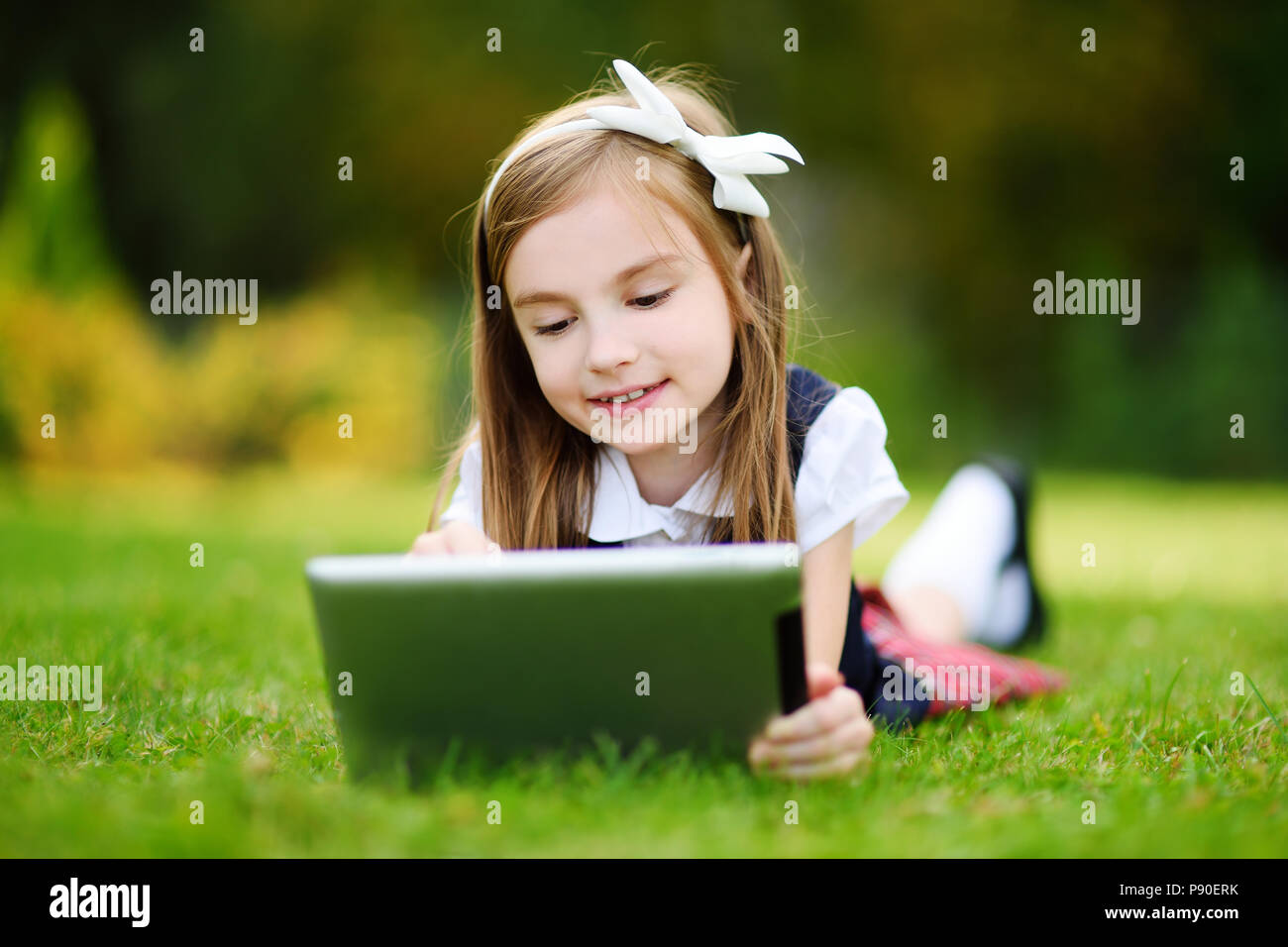 Adorable little girl using computer tablet while sitting on a grass on ...