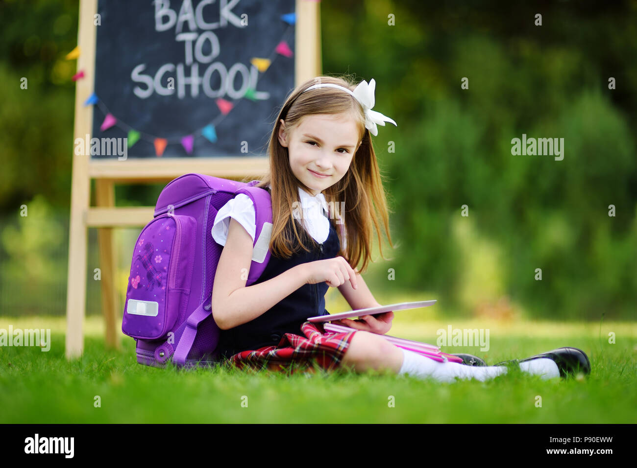 Adorable little girl using computer tablet while sitting on a grass on ...