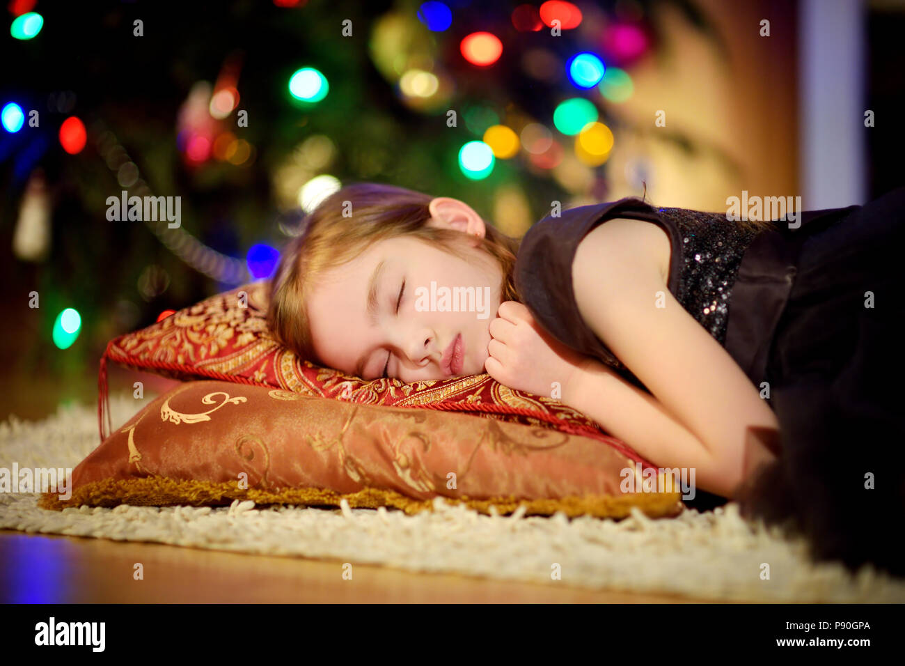 Adorable little girl sleeping under the Christmas tree by a fireplace ...