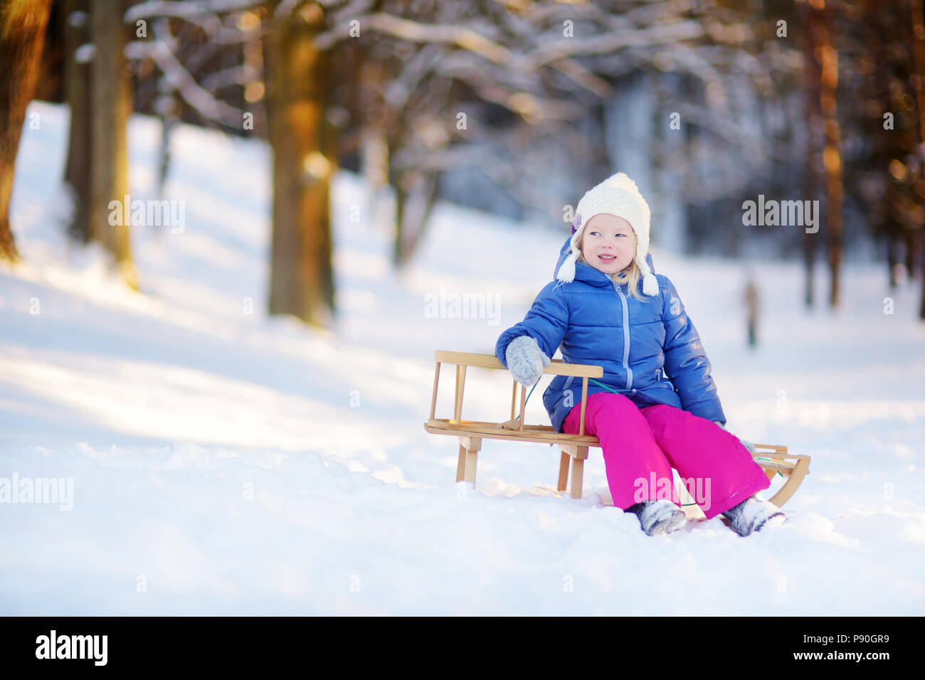 Funny little girl having fun with a sleight in beautiful winter park ...