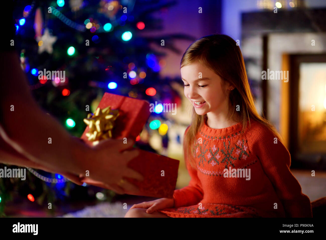 Happy little girl getting a Christmas gift from her parent by a ...