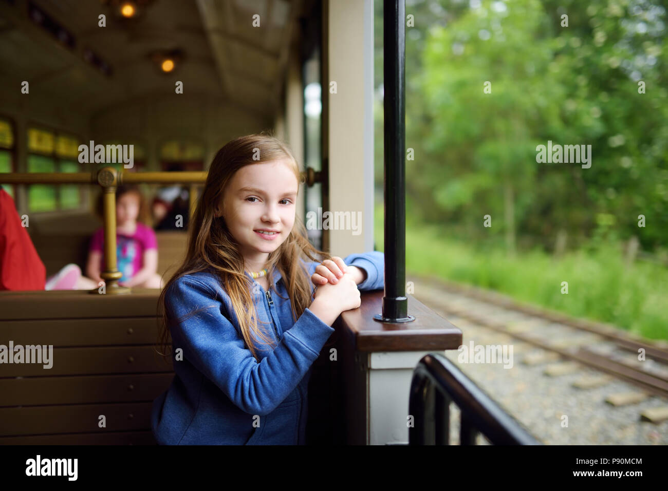 Happy little girl riding a train in a theme park or funfair on summer ...