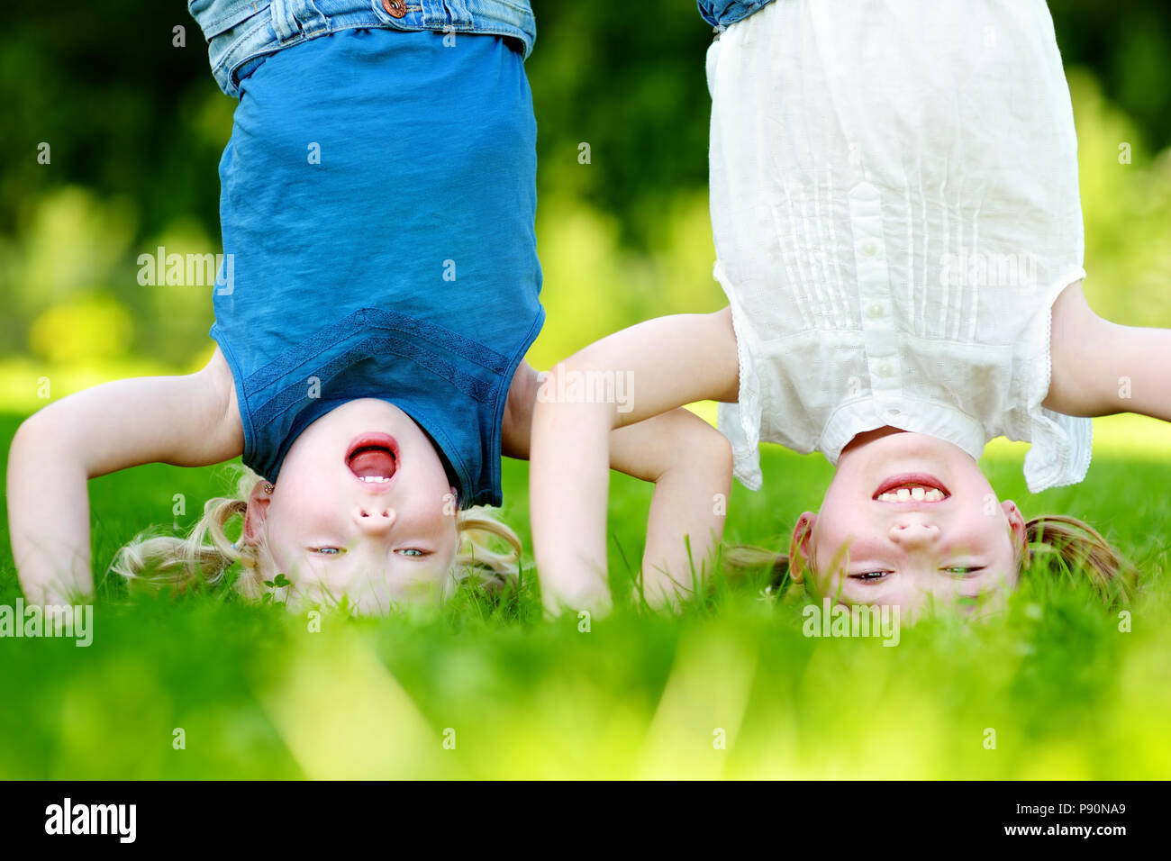 Happy children playing head over heels on green grass in spring park ...