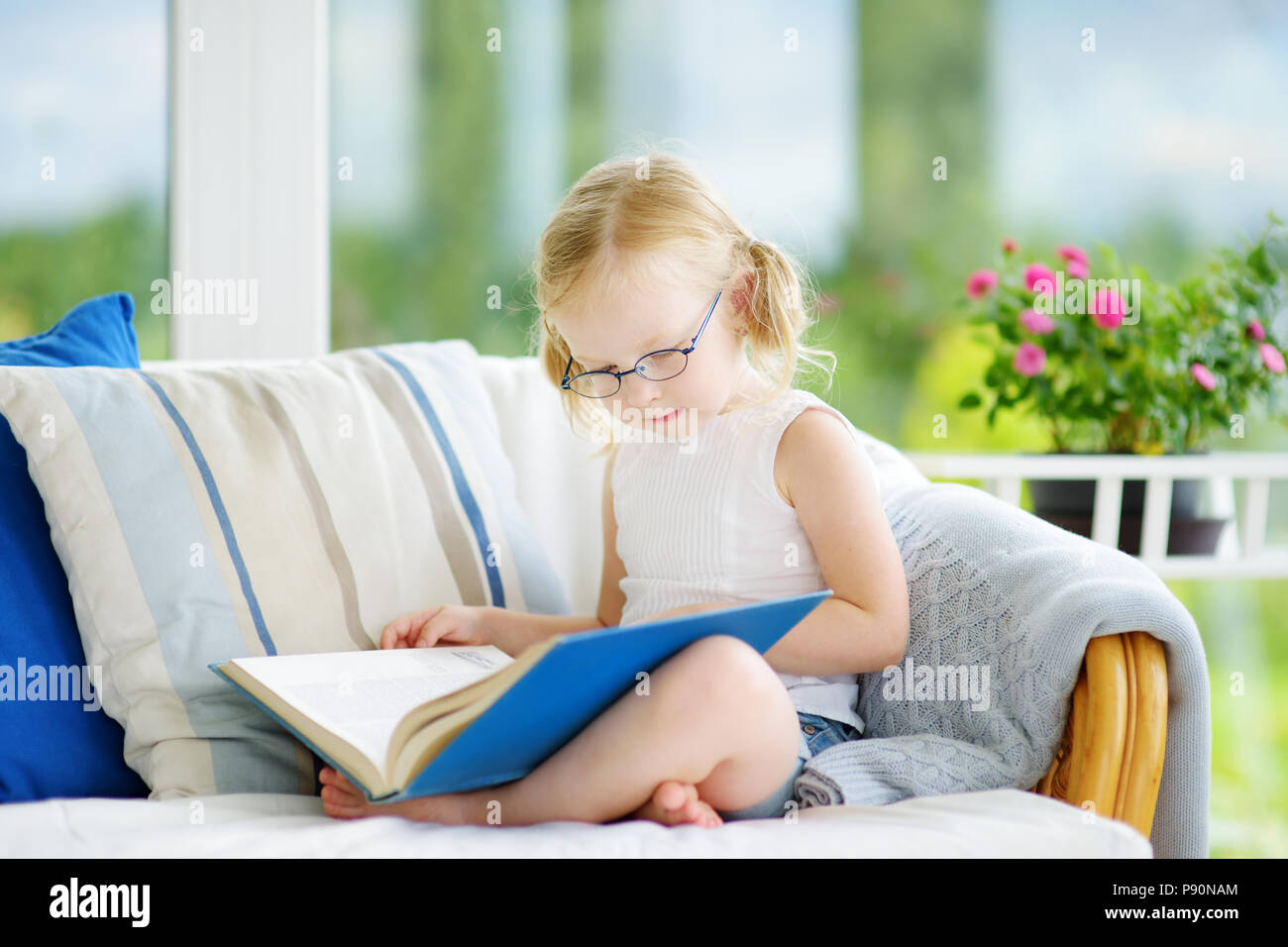 Adorable little girl wearing eyeglasses reading a book in white living ...