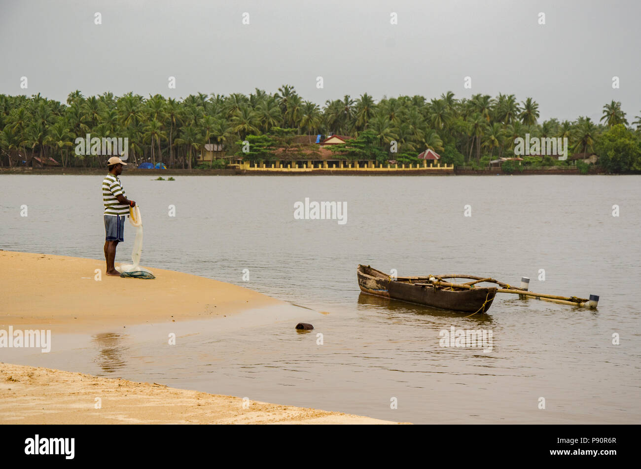 Fisherman folding fishing net beside an anchored canoe on the beautiful ...