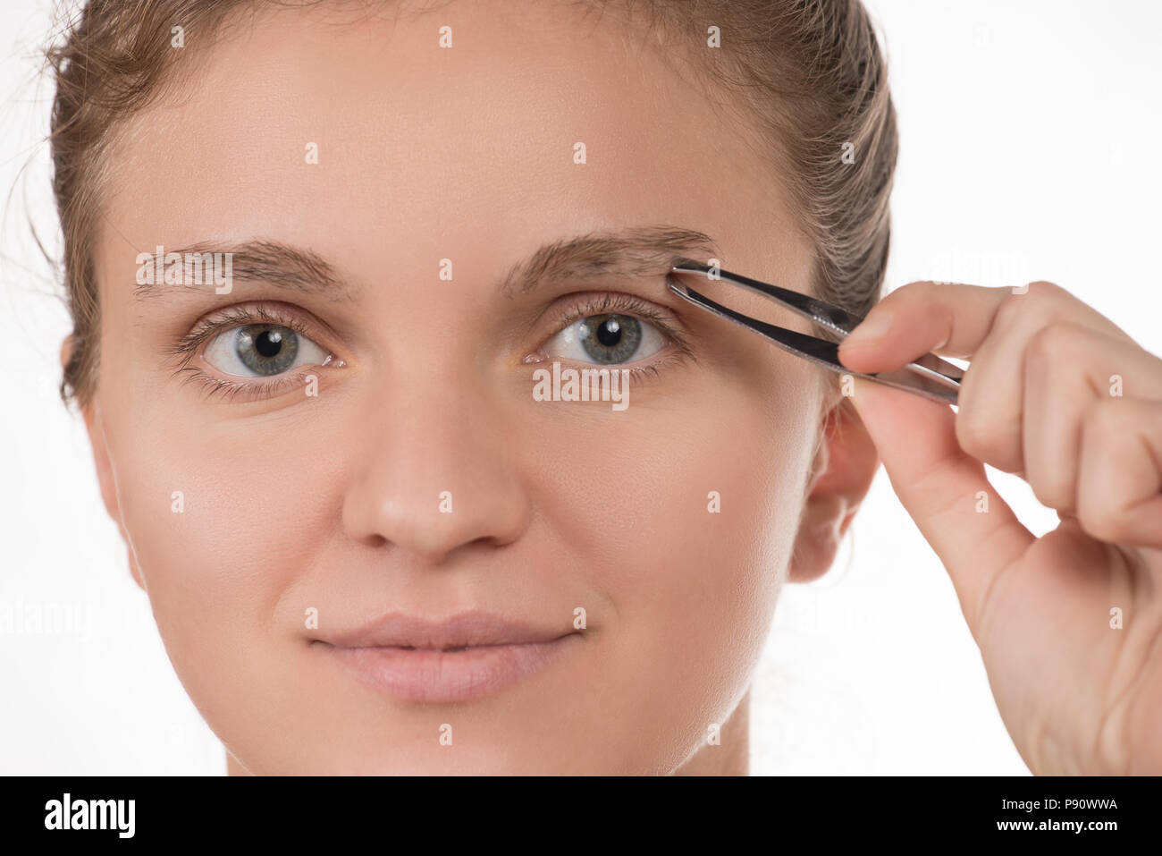 Young beautiful girl pulls out her eyebrows with tweezers metal on a ...