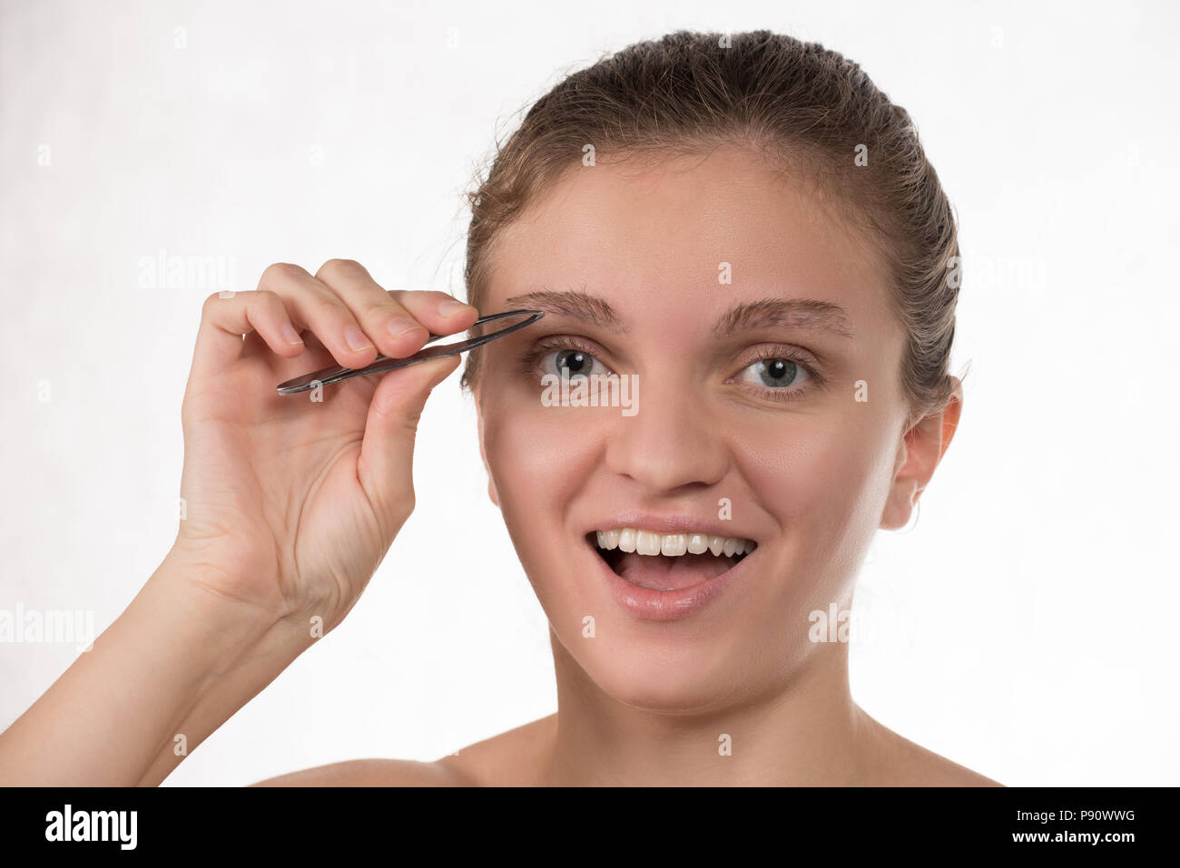 Young beautiful girl pulls out her eyebrows with tweezers metal on a ...