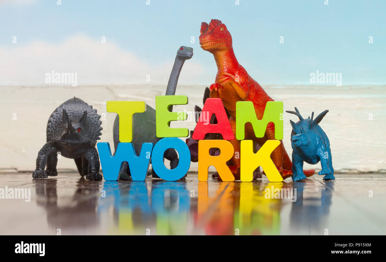 the word TEAM WORK with wooden letters and 5 toy dinosaurs on a wooden ...