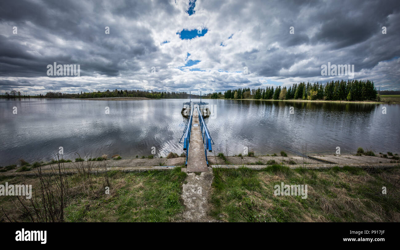 Symmetrical view of a narrow pier leading into a calm lake under ...
