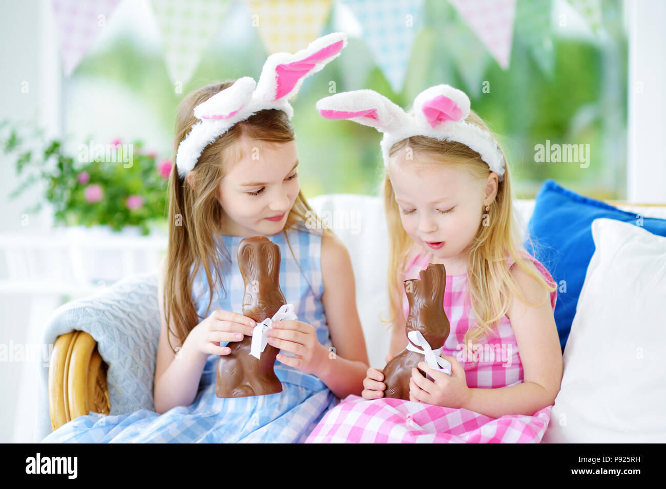Two cute little sisters wearing bunny ears eating chocolate Easter ...