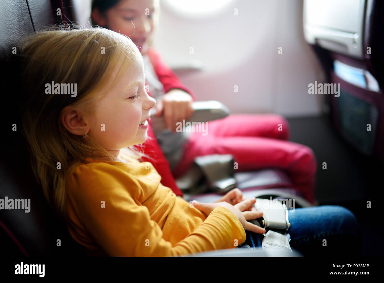 Two adorable little girls traveling by an airplane. Children sitting by ...