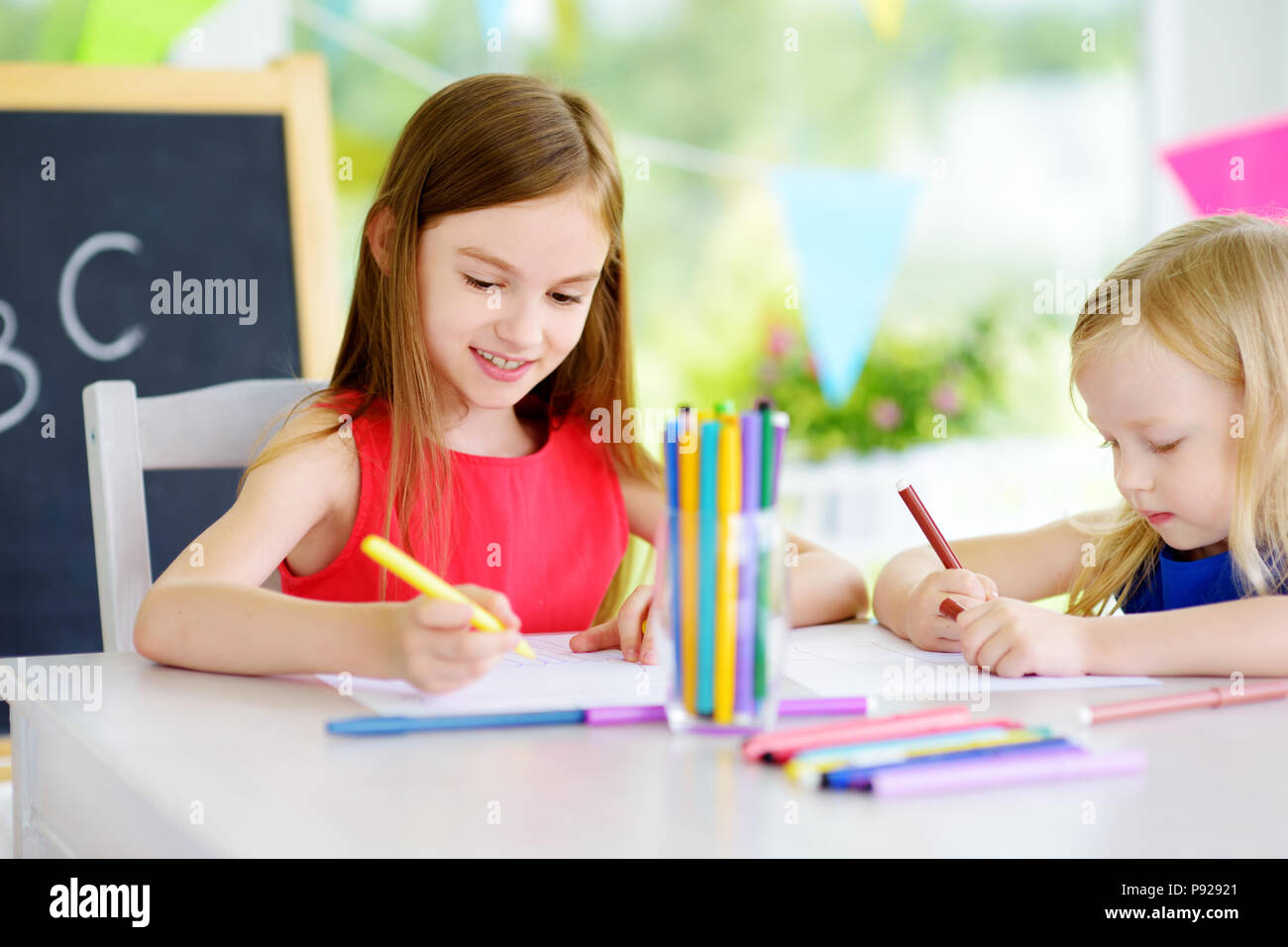Two cute little sisters drawing with colorful pencils at a daycare ...