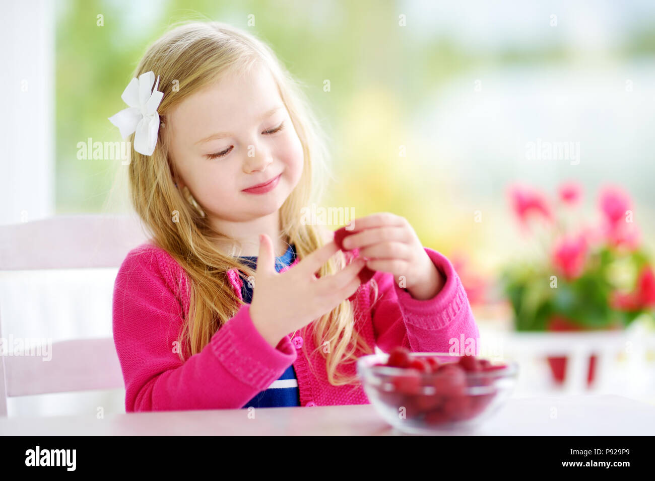 Pretty little girl eating raspberries at home. Cute child enjoying her ...