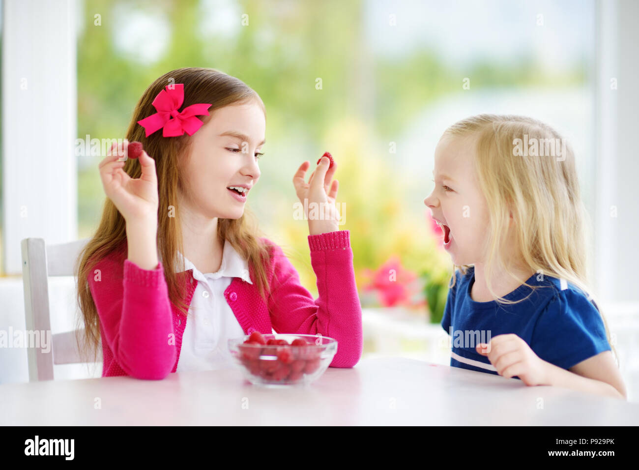 Two pretty little girls eating raspberries at home. Cute children ...