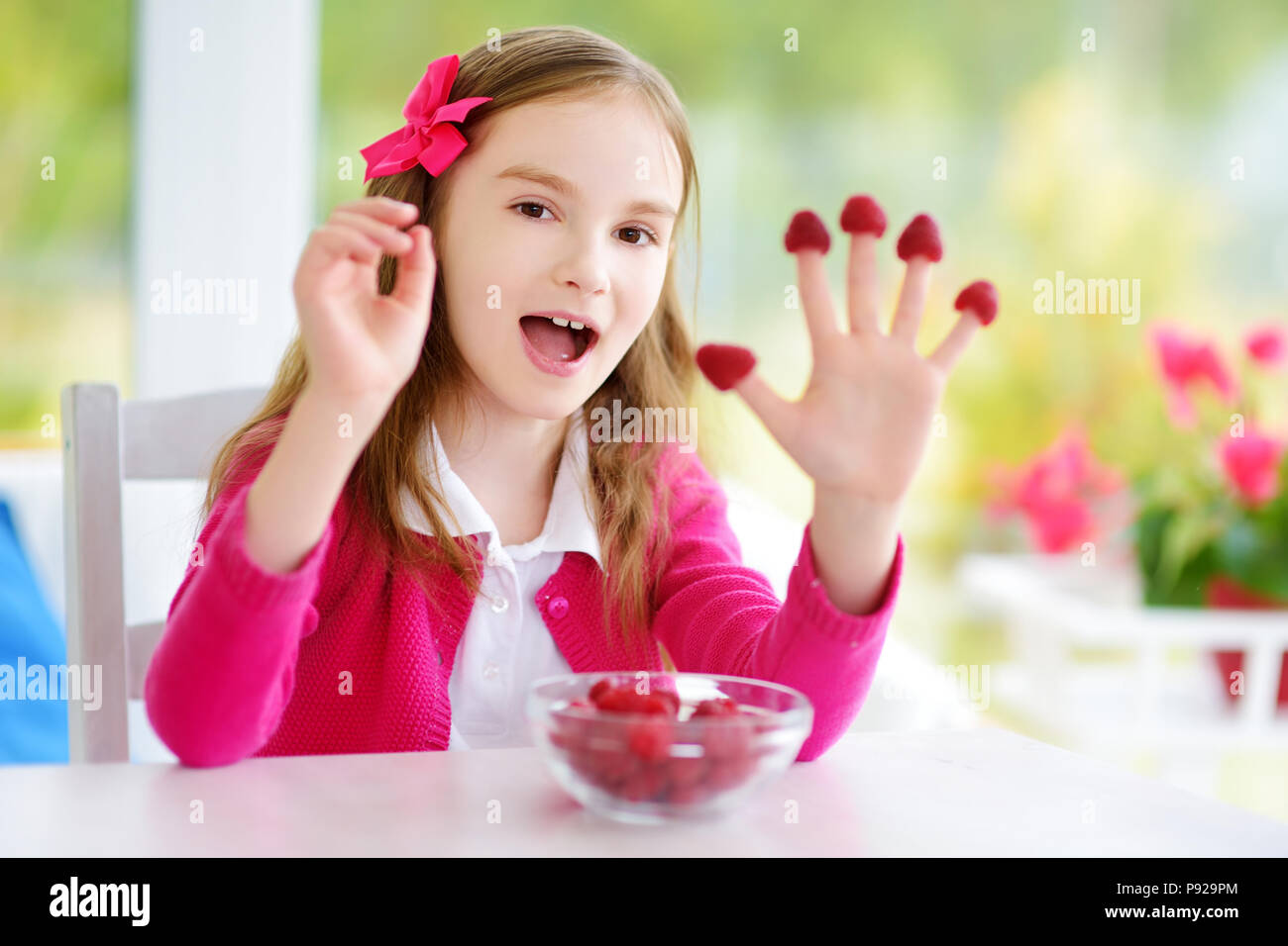 Pretty little girl eating raspberries at home. Cute child enjoying her ...