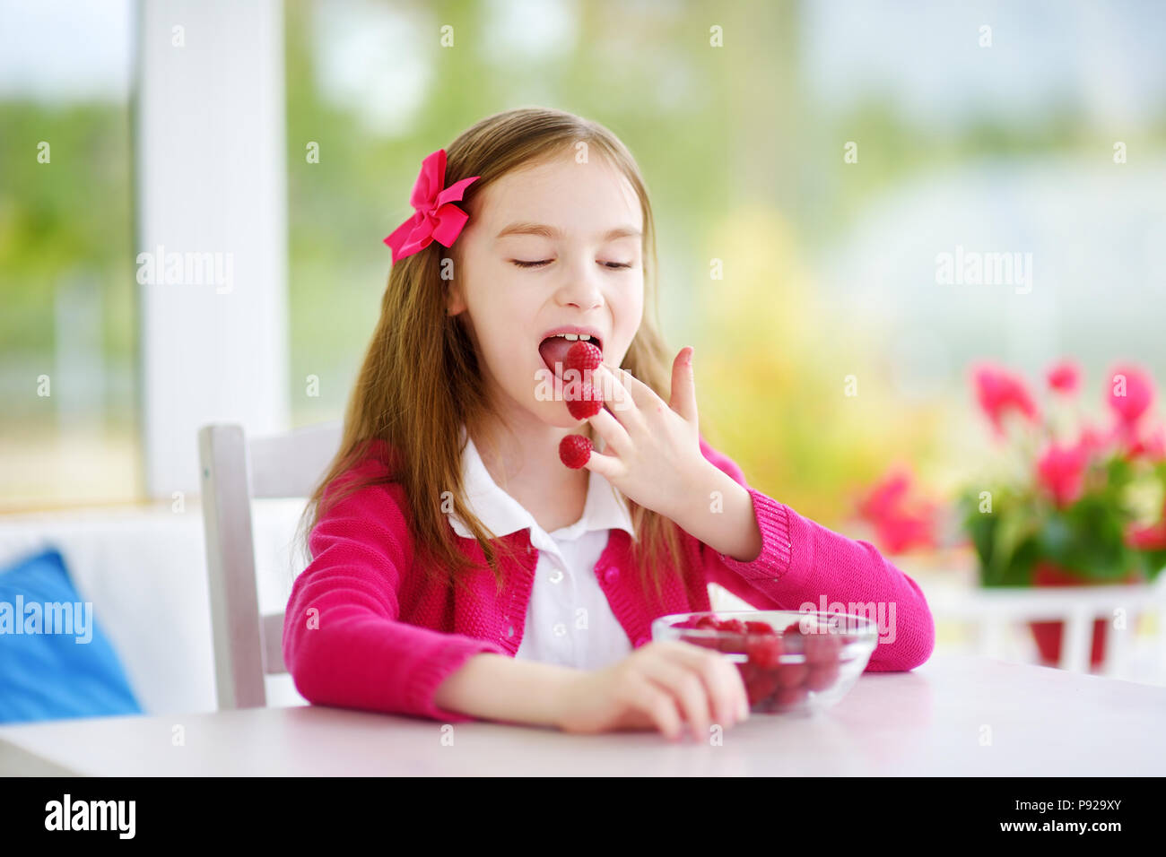 Pretty little girl eating raspberries at home. Cute child enjoying her ...