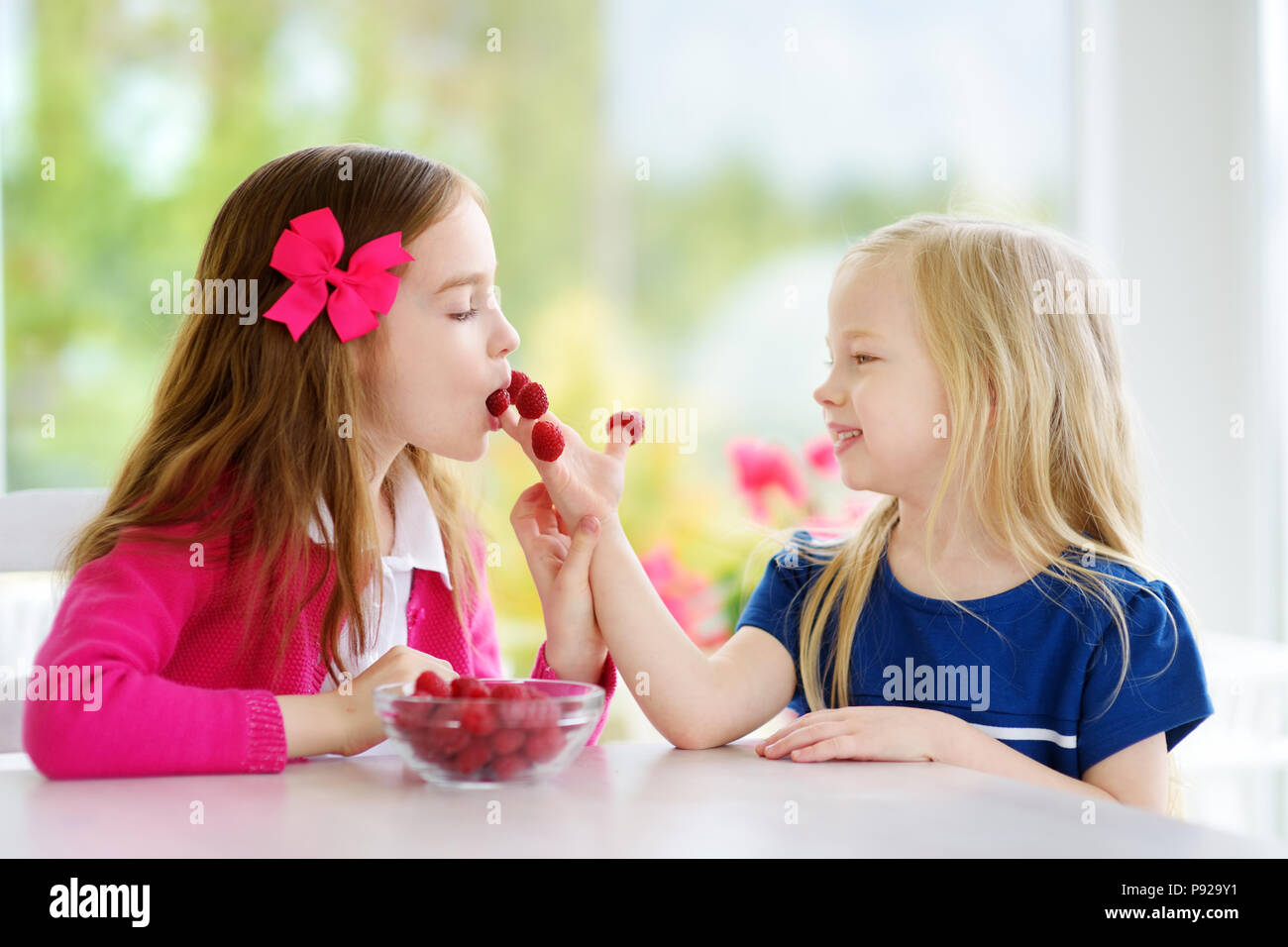 Two pretty little girls eating raspberries at home. Cute children ...