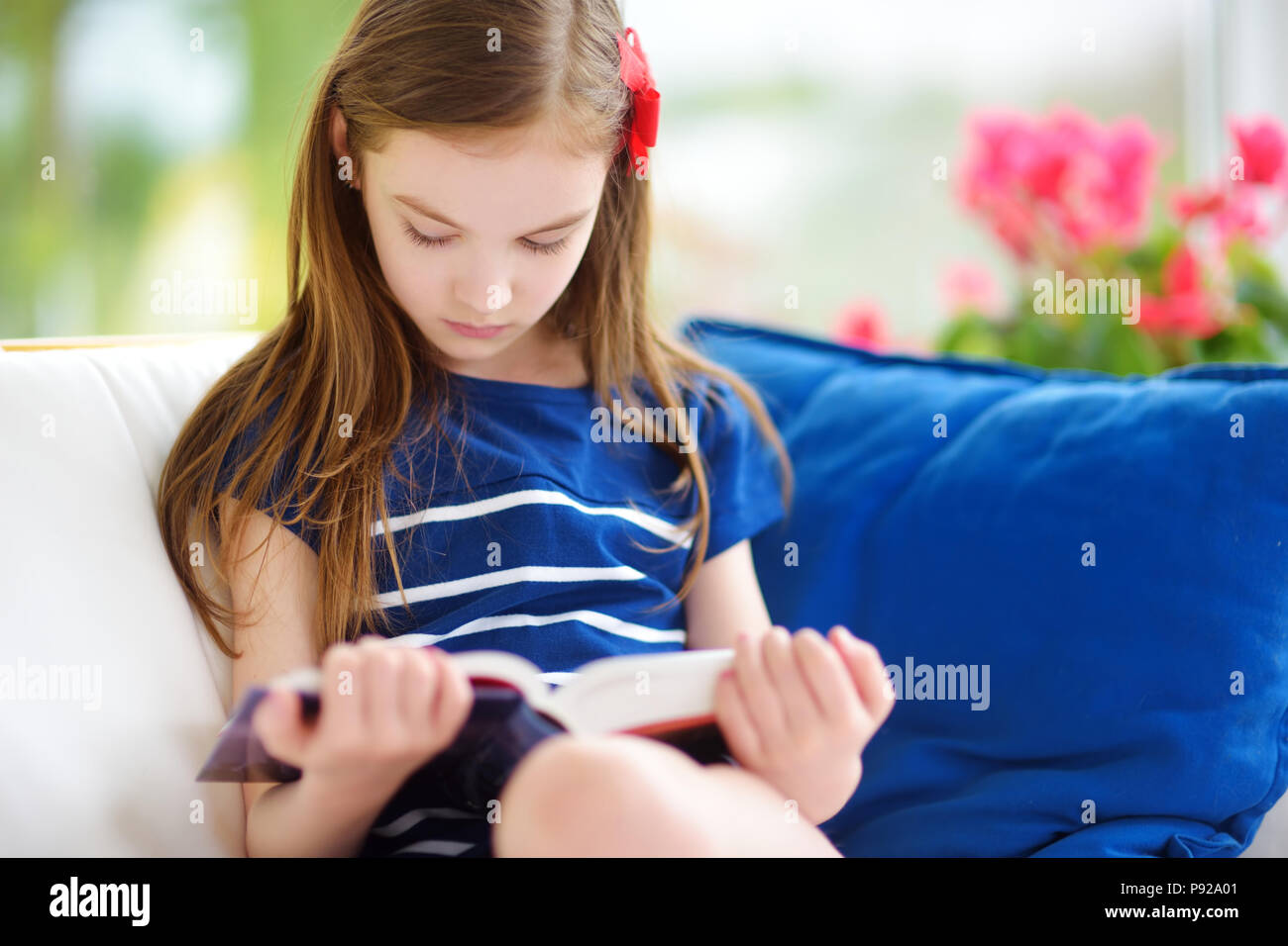 Adorable little girl reading a book in white living room on beautiful ...