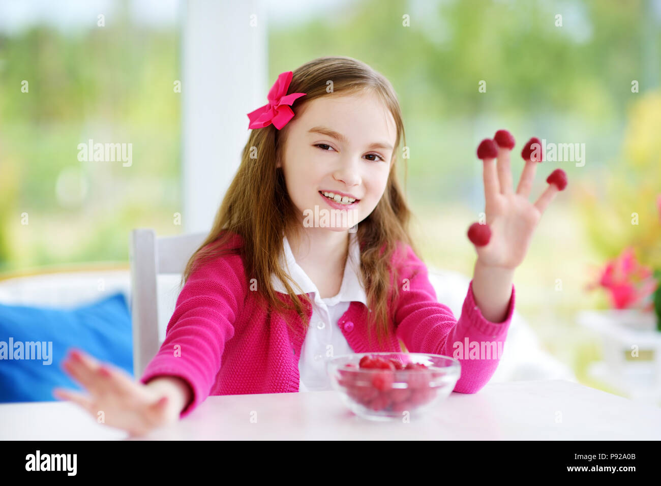 Pretty little girl eating raspberries at home. Cute child enjoying her ...