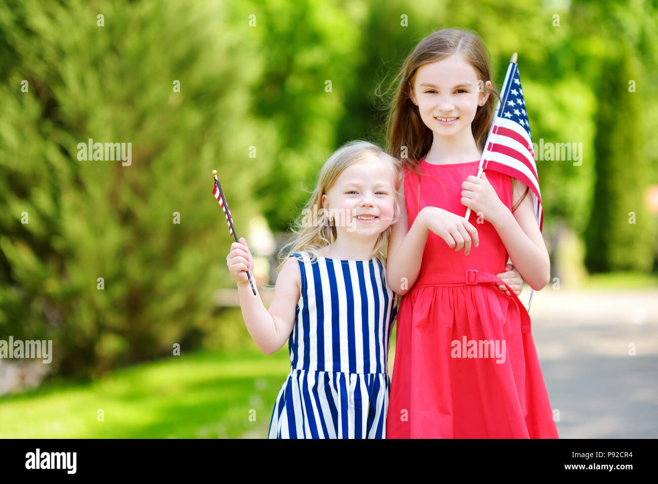 Two adorable little sisters holding american flags outdoors on ...