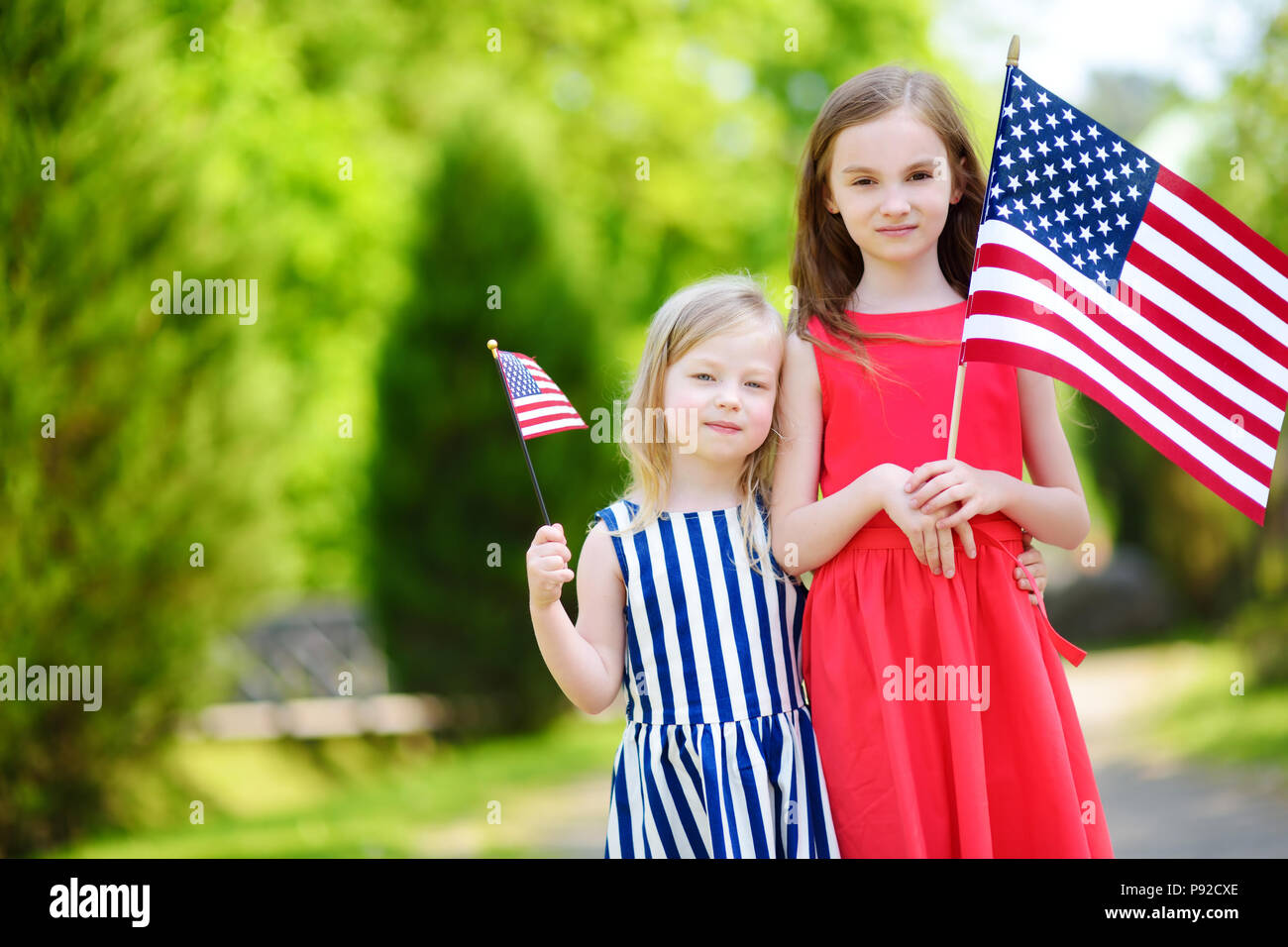 Two adorable little sisters holding american flags outdoors on ...