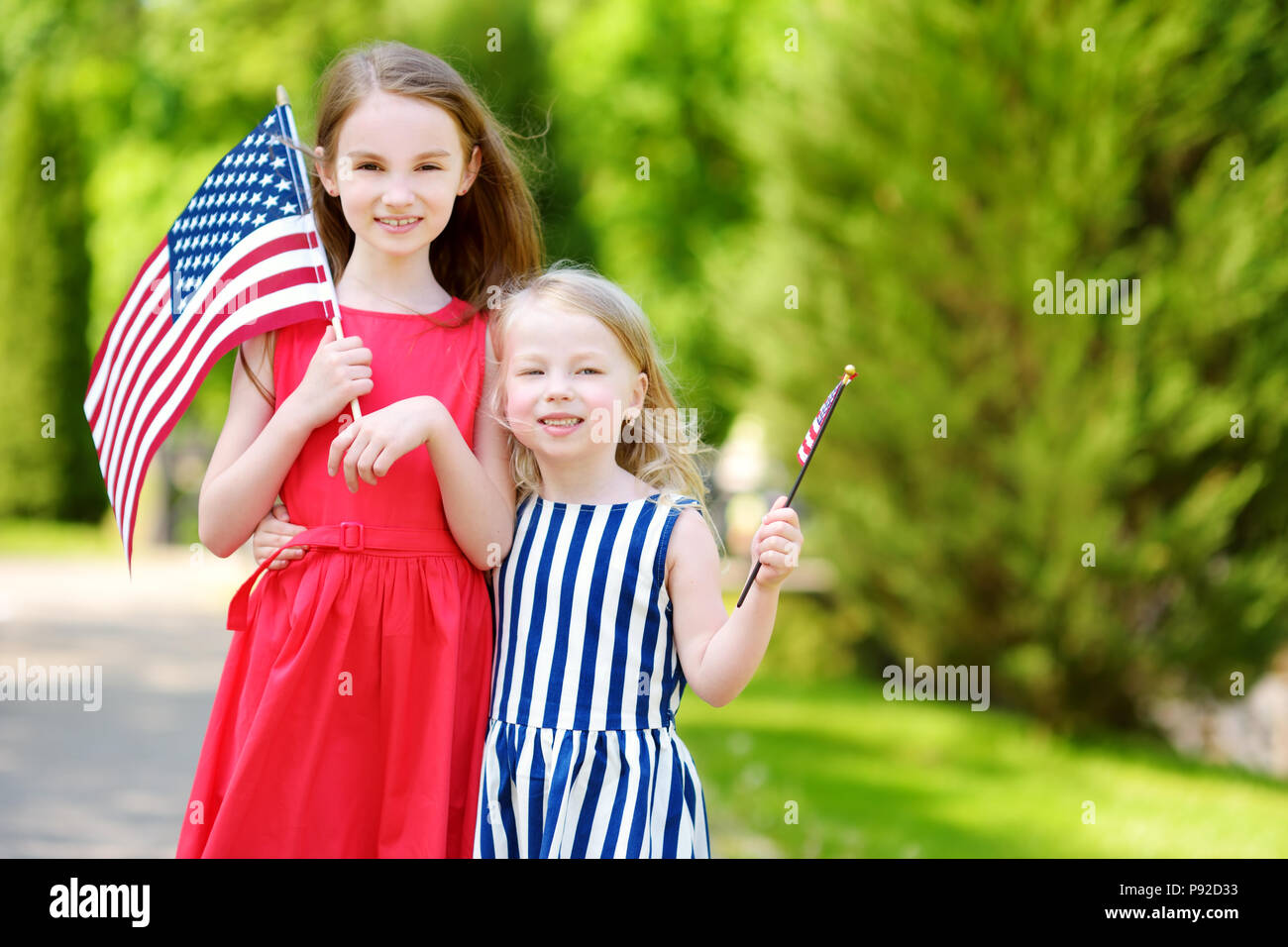 Two adorable little sisters holding american flags outdoors on ...